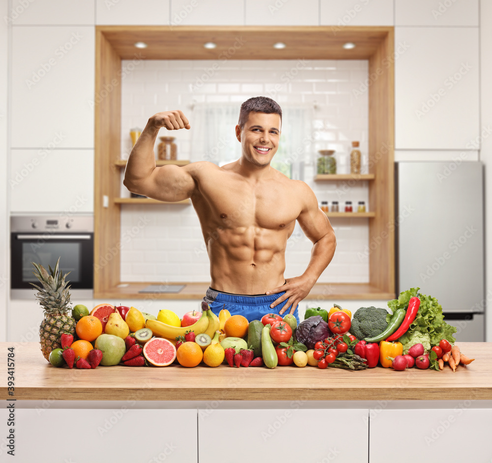 Muscular man flexing biceps muscle and posing with a pile of fruits and ...