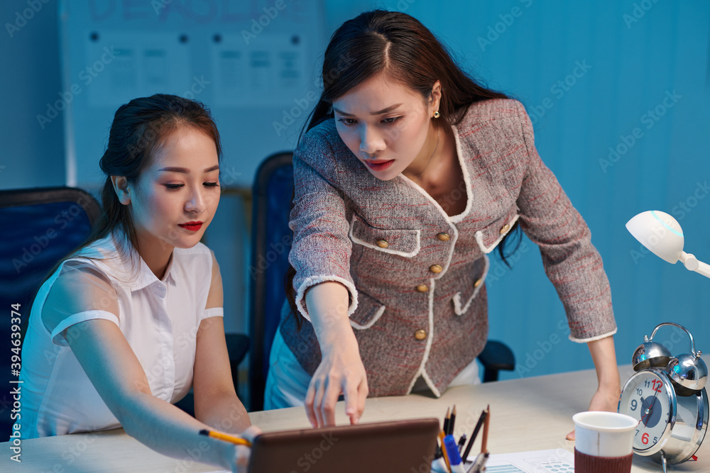 Angry pretty young businesswoman pointing at screen of tablet computer ...