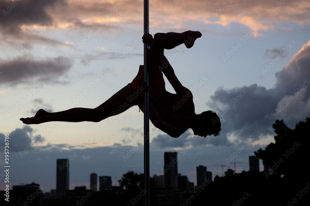 Muscular male pole dancer, holding a pose on a pole set outdoors ...
