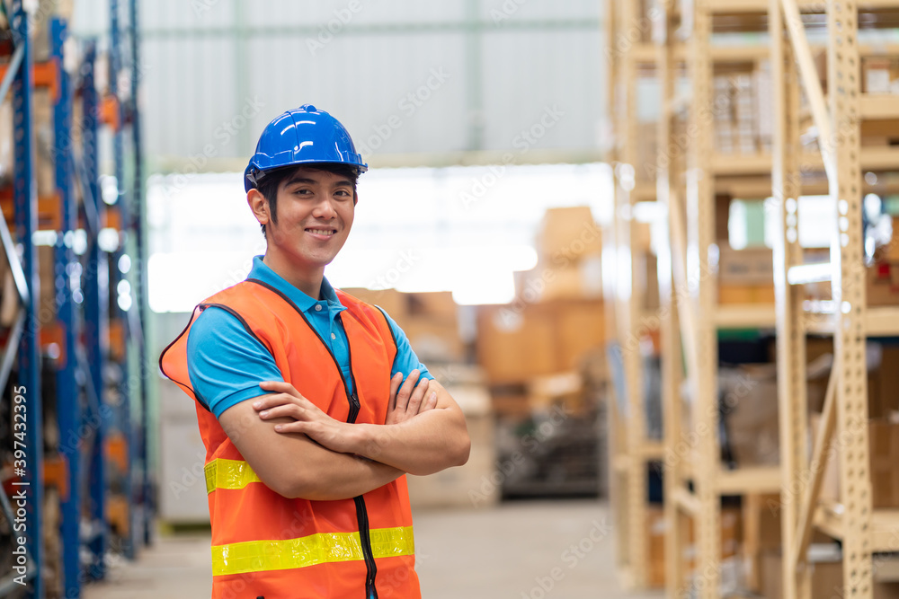 Confident smiling Asian male warehouse worker in safety vest and helmet ...