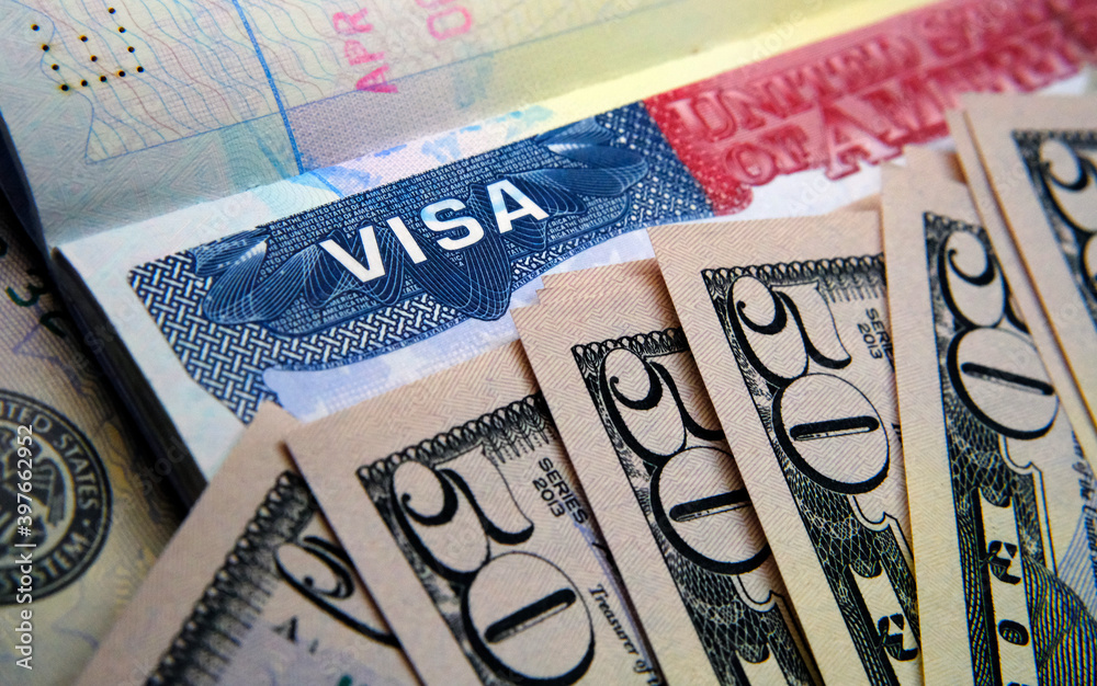 United States visa sticker seen in passport and dollar banknotes placed ...