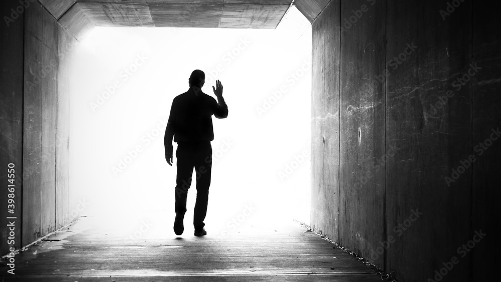 A single male in a dark tunnel exiting and walking towards a bright ...