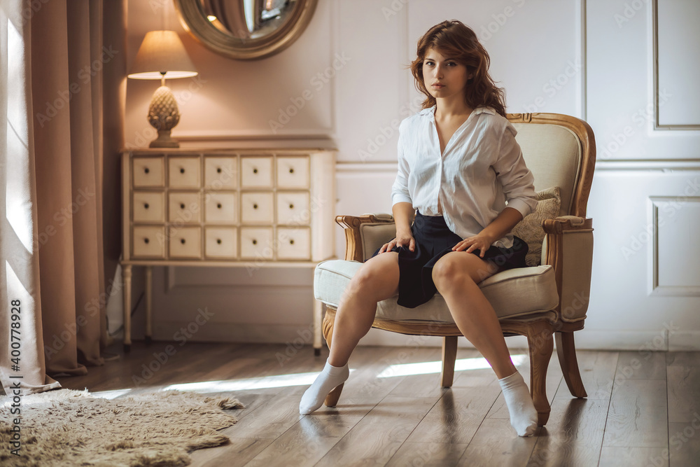 The girl is sitting on a chair in a short skirt with her legs spread ...