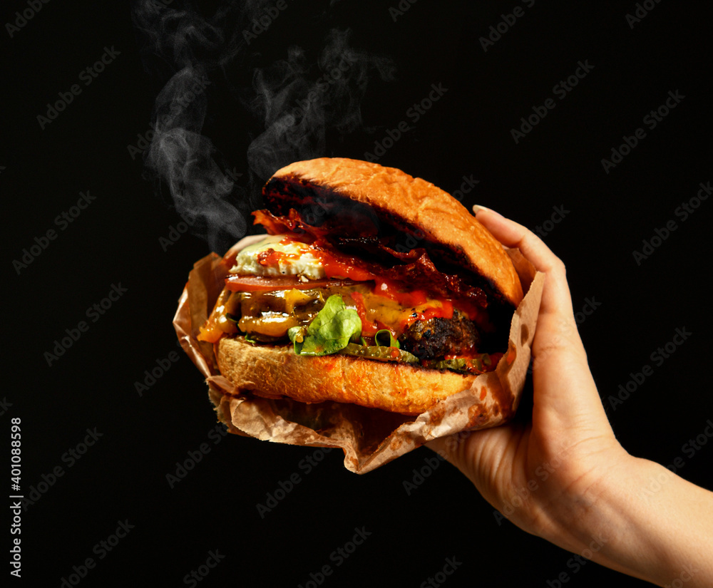 Woman hands hold big cheeseburger barbeque sandwich with marble beef cheese bacon with steam ...