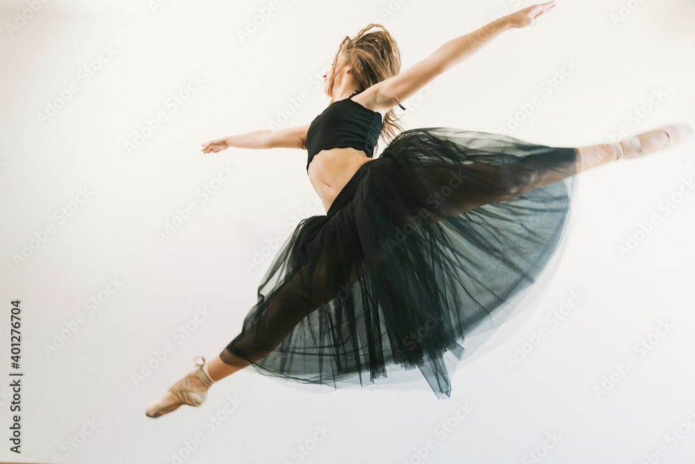 Side view of ballerina in black tutu jumping in splits with ...
