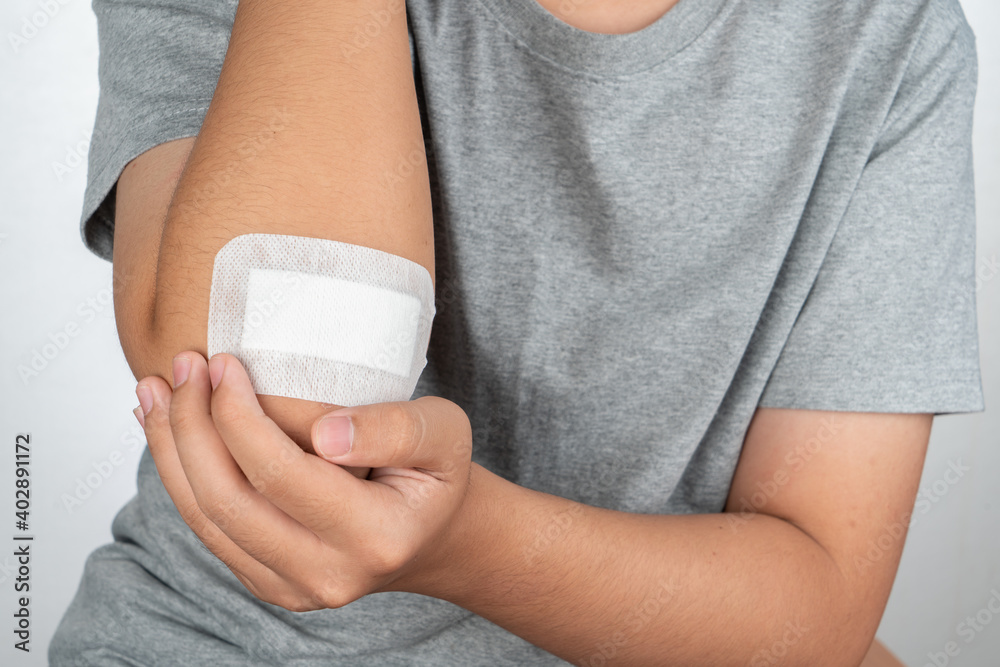Asian boy putting sticking plaster on injured elbow skin by himself ...