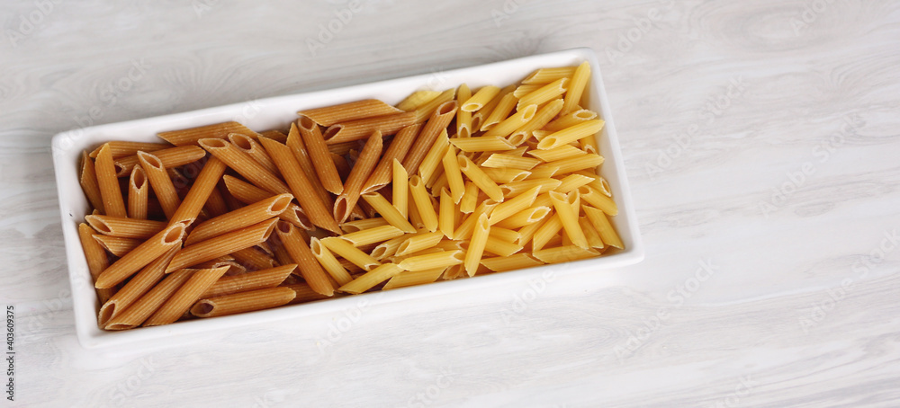 Mix of wholegrain penne and white mini penne in ceramic plane top view ...
