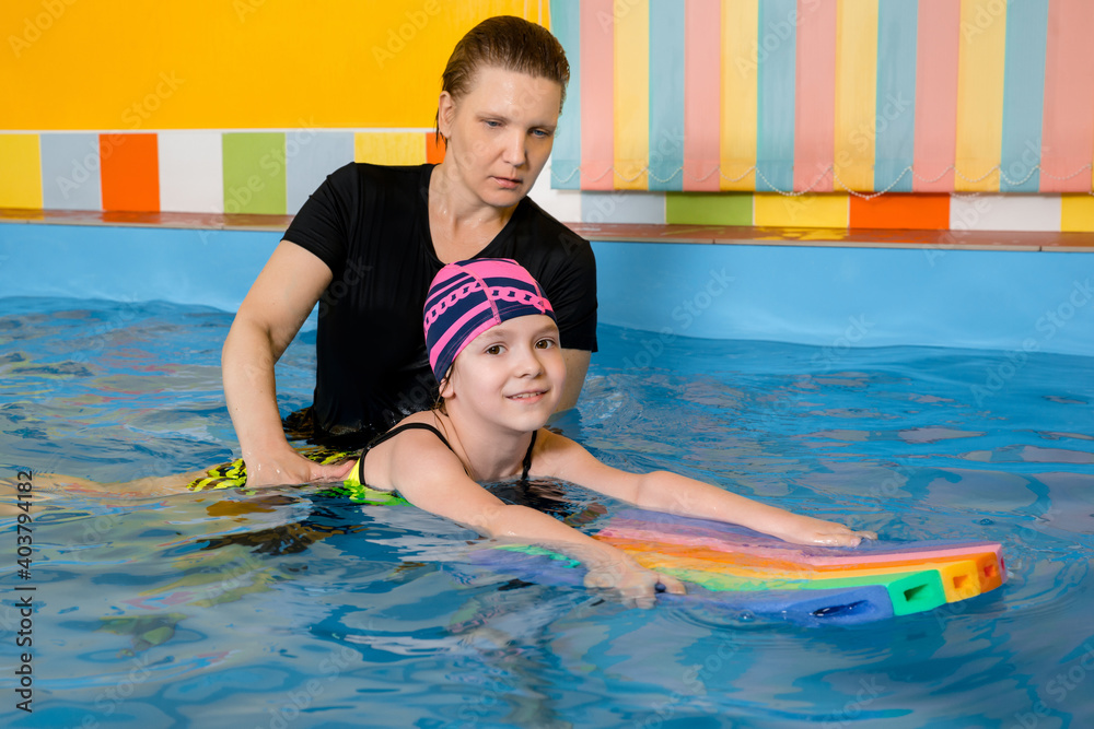 Coach teaching kid in indoor swimming pool how to swim with flutter ...