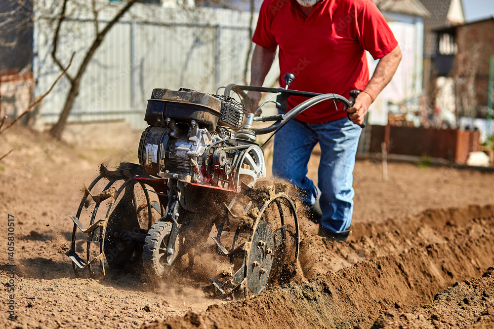 Gardener man cultivate ground soil with tiller tractor or rototiller ...