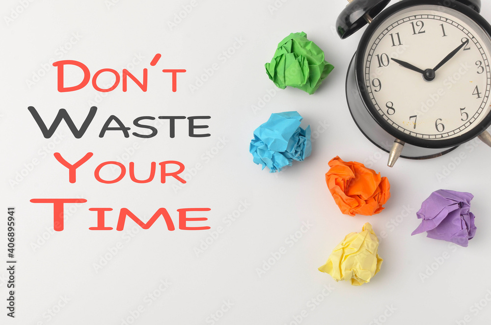 Dont Waste Your time written with alarm clock and paper trash on white ...