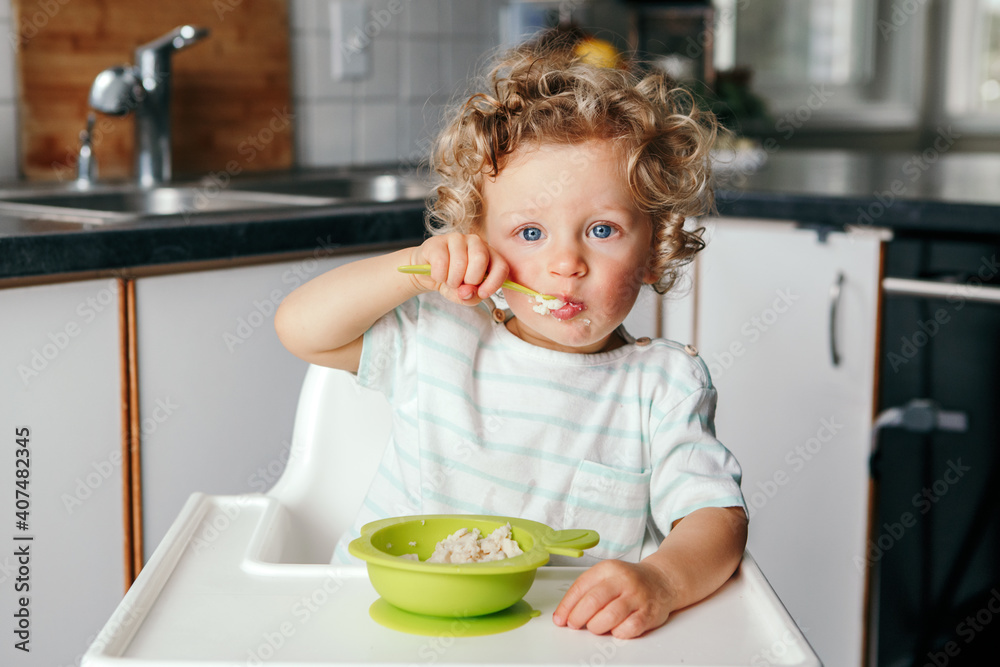 Cute adorable Caucasian curly kid boy sitting in high chair eating ...