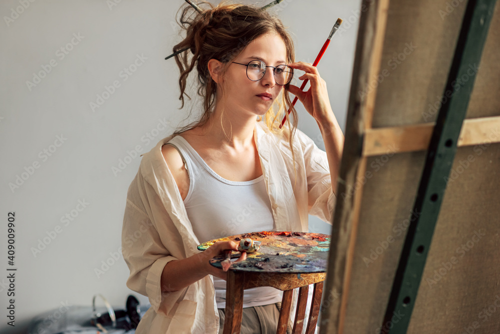 Horizontal candid shot of a girl artist standing next to the easel with ...