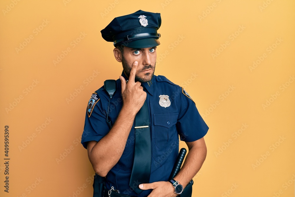 Handsome hispanic man wearing police uniform pointing to the eye ...