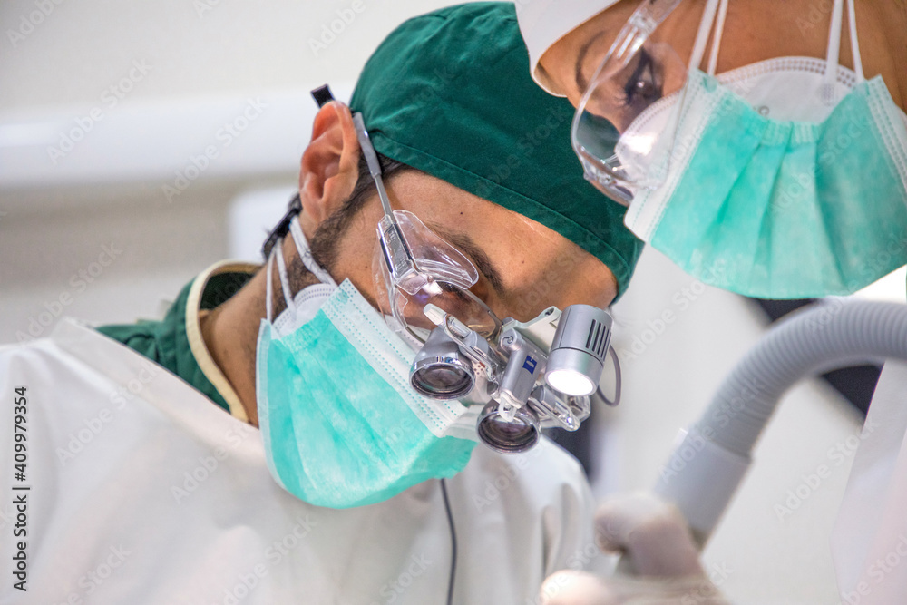 Dentists in masks and uniform operating patient lying in dental chair ...