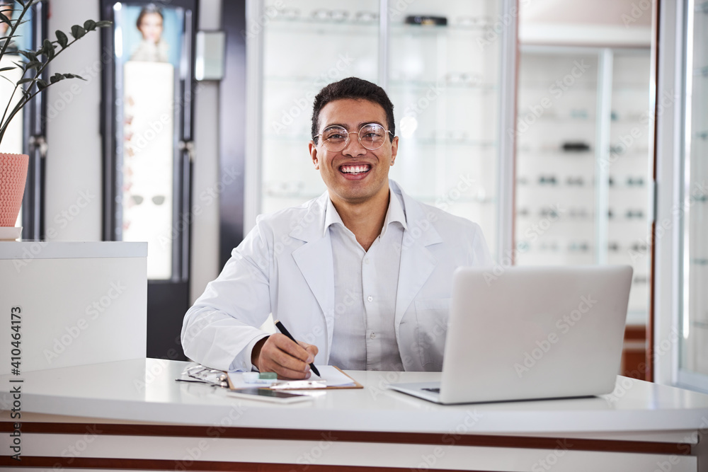 Foto de Stock Smiling bespectacled optometrist seated at the table in ...