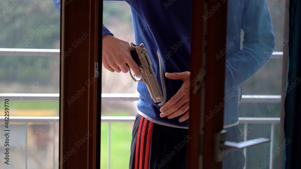 man thief enters the house from the balcony window with a gun pistol ...