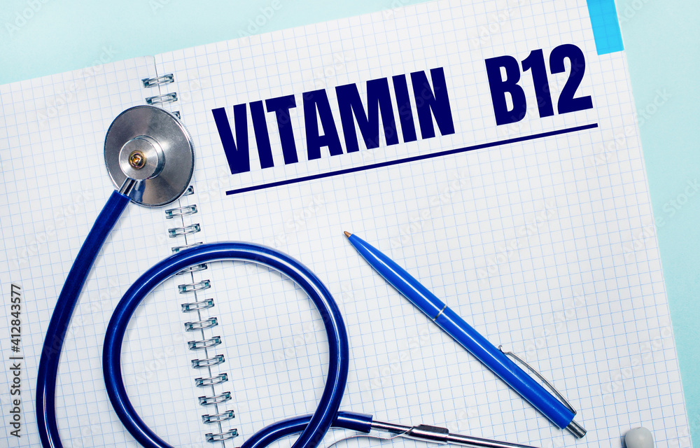 On a light blue background, an open notebook with the word VITAMIN B12 ...