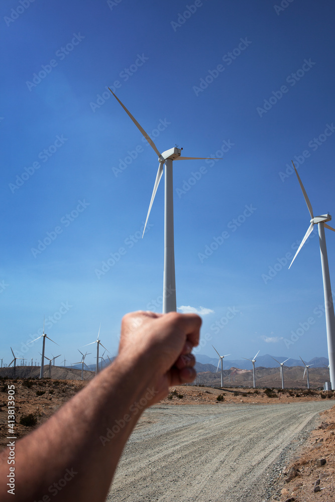 Optical illusion of man's hand holding wind turbine against blue sky ...