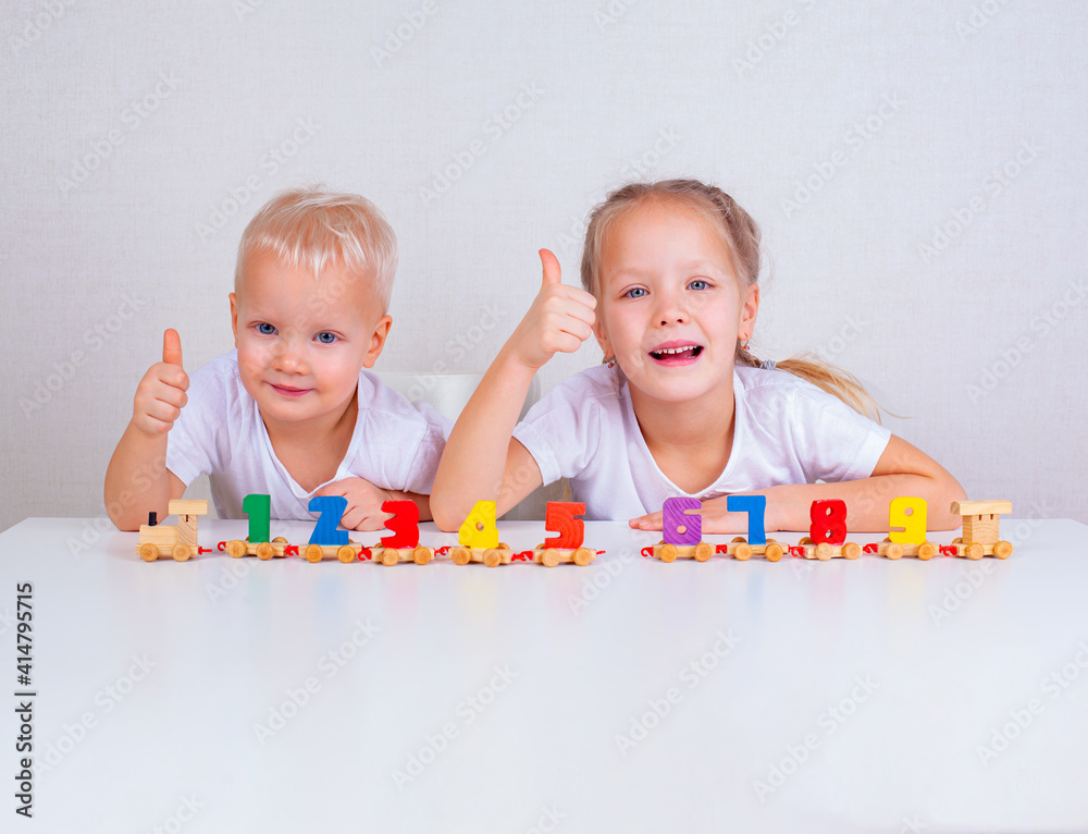 Beautiful brother and sister are sitting at the table learning numbers ...