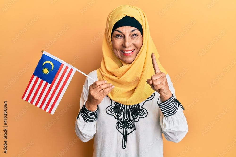 Middle age hispanic woman wearing hijab holding malaysia flag smiling ...