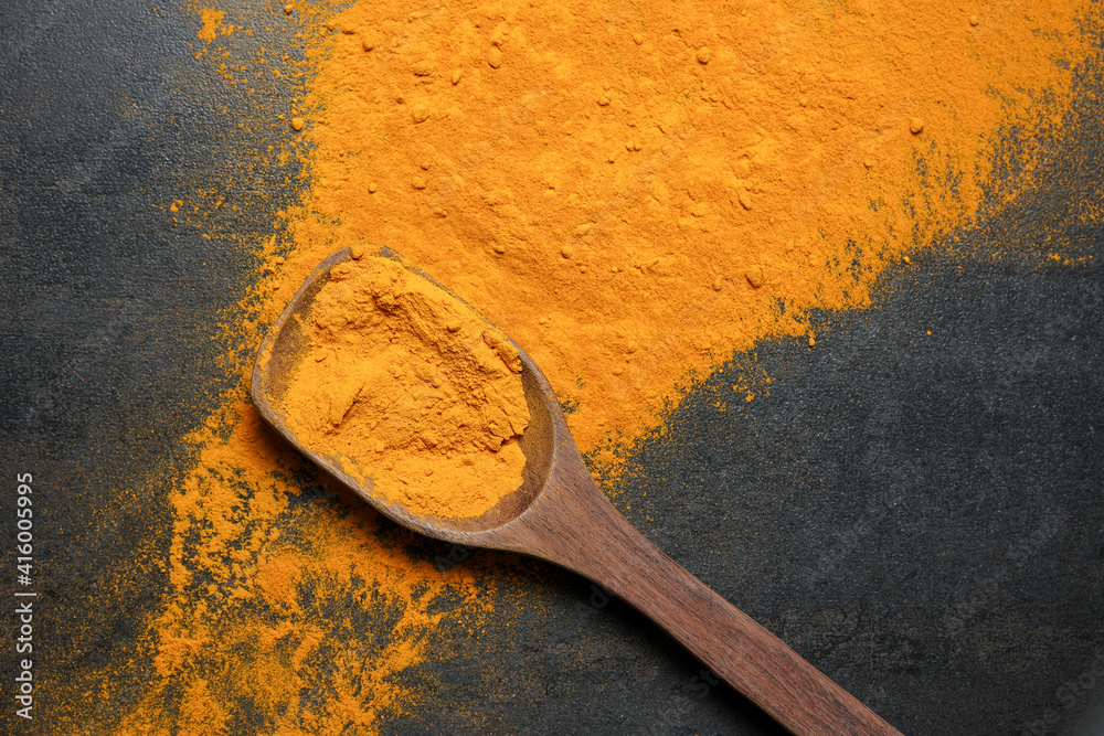 Indian spices turmeric powder in wooden spoon scattered on black ...