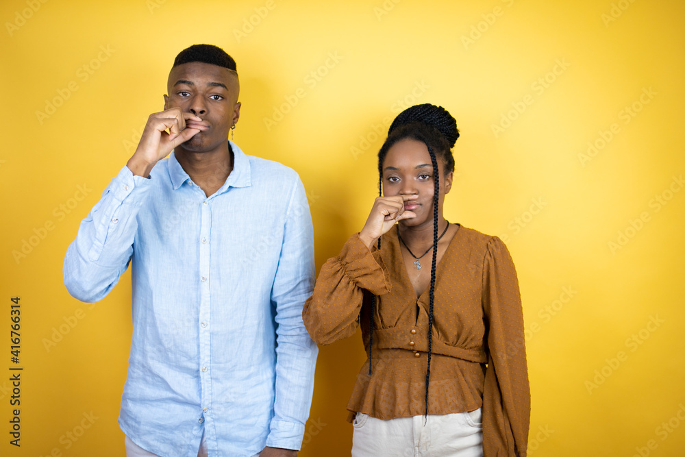 Young african american couple standing over yellow background mouth and ...