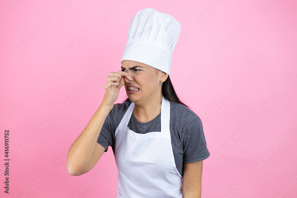 Young hispanic woman wearing baker uniform over pink background ...