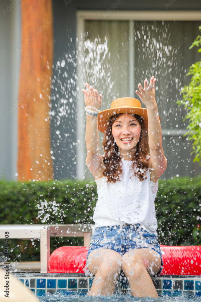 Young beautiful woman making water splash at the pool. Asian girl ...