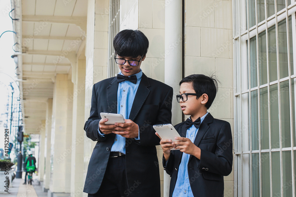Two brothers with vintage black suit using tablet while smiling. Little ...