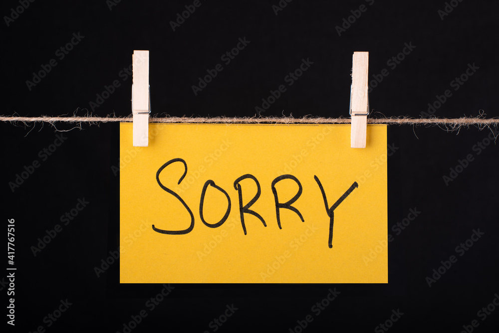 Sorry word written on a Yellow color sticky note hanging with a wire on ...