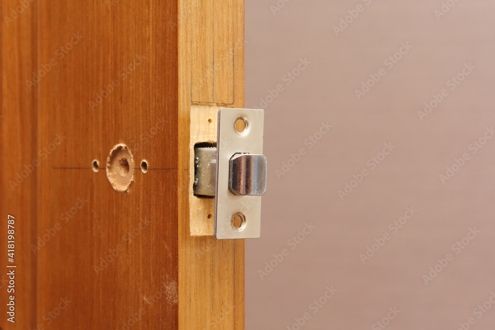 Inserting door latch in end hole close-up. Fitting door lock in panel ...