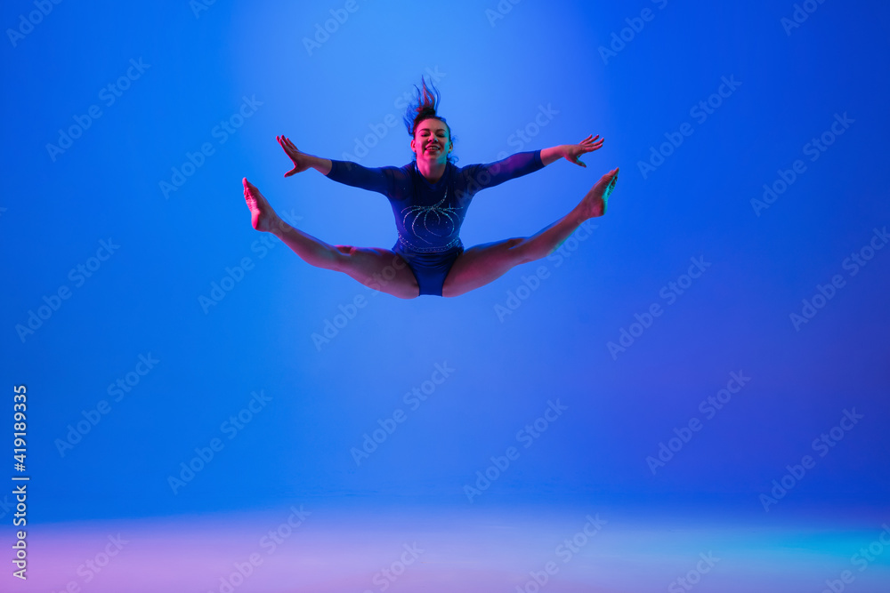 Jumping high. Young flexible girl isolated on blue studio background in ...