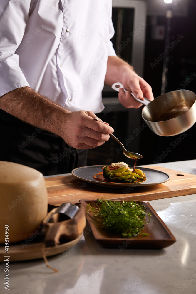 Professional cook in uniform add some spices to dish, decorating ...
