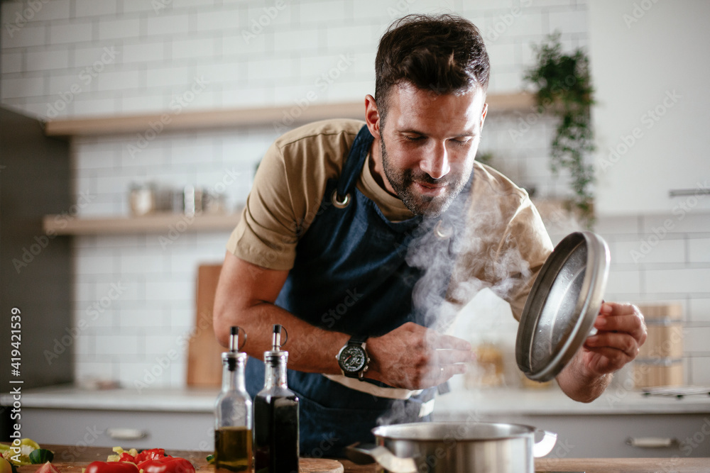 Handsome man preparing pasta in the kitchen. Guy cooking a tasty meal ...