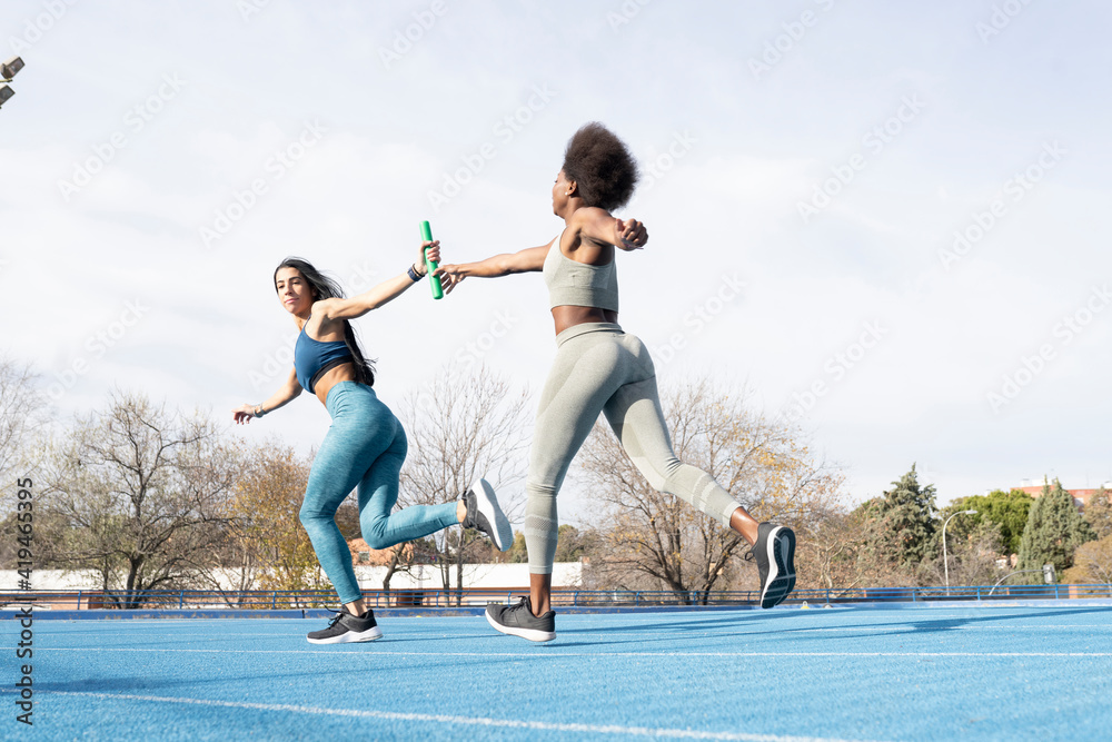 Fit multiracial female athletes passing baton while running along track ...