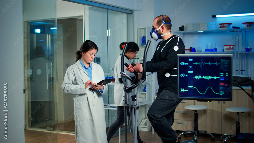 Sportsman with mask running on cross trainer in sports science ...