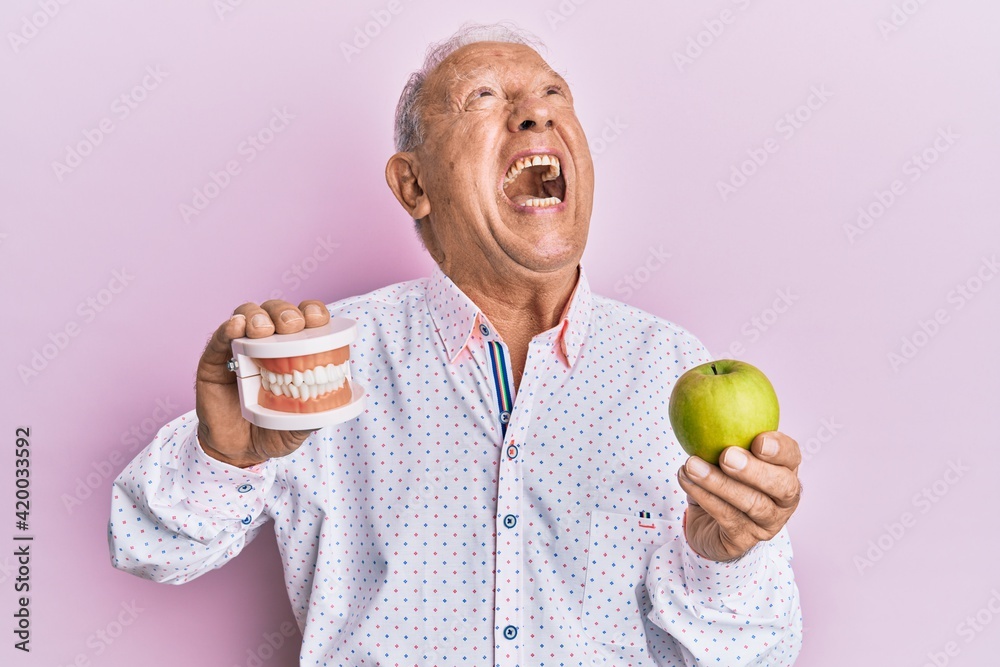 Senior caucasian man holding denture and green apple angry and mad ...