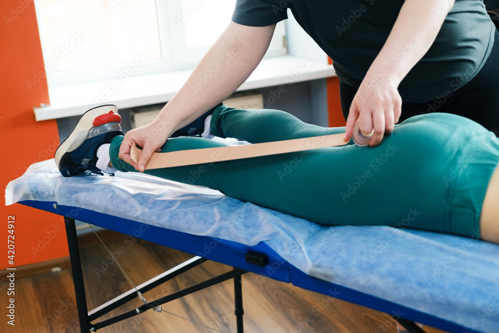 The physiotherapist massages the injured leg of the athlete lying on ...