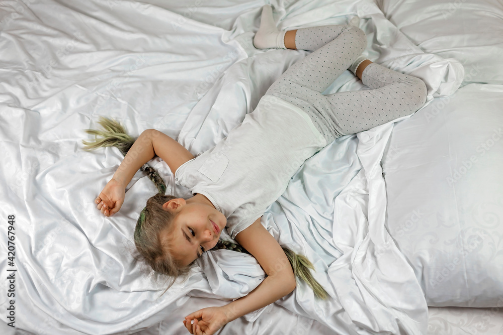 Cute awaking girl in white clothes with two braids lying on the bed in ...