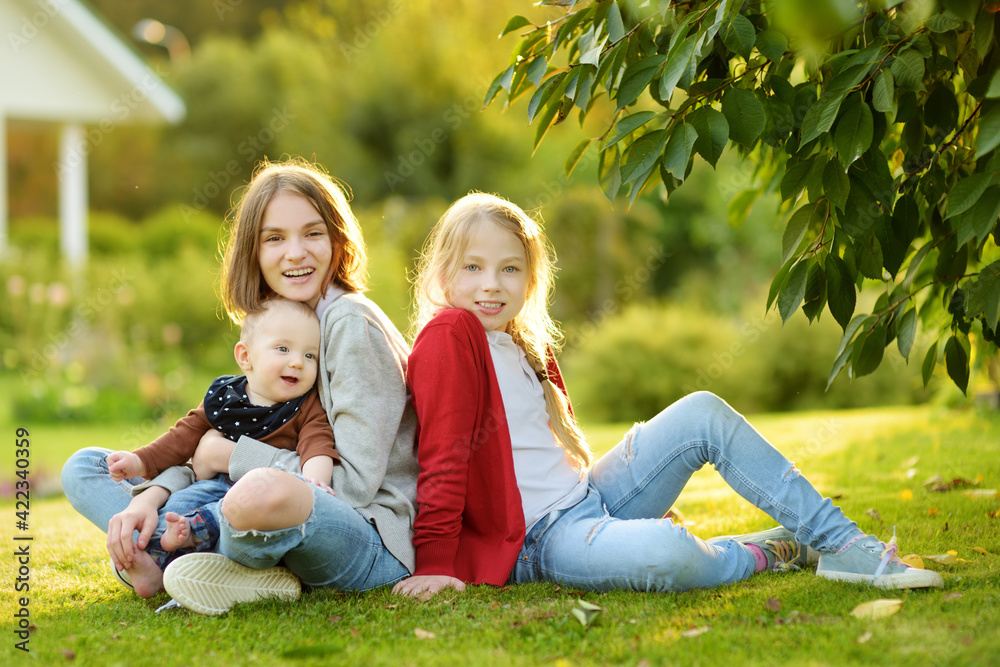 Two big sisters and their infant brother having fun outdoors. Two young ...