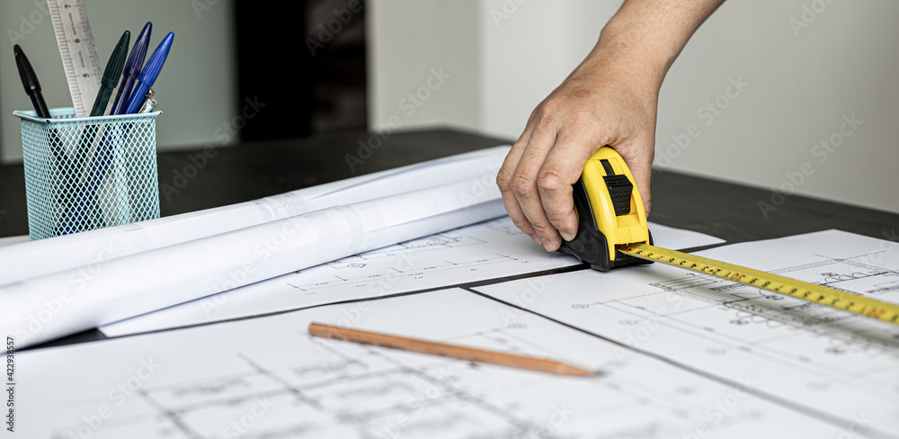 An engineer is using a tape measure to measure the plans of the house ...