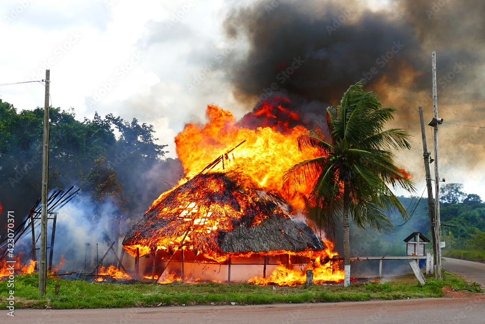 In bright flames burning indian hut made of wood and dried palm leaves ...