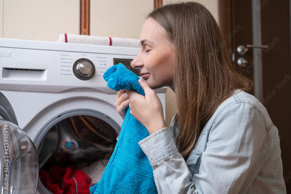 Young woman putting laundry into washing machine. Woman washing laundry ...
