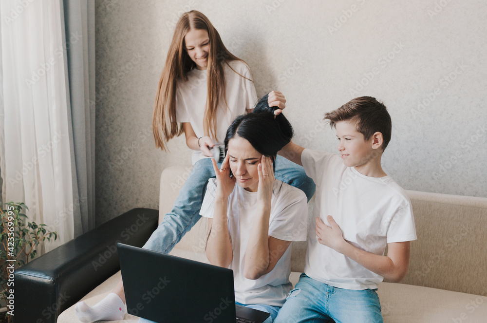 An irritated mother sits on the couch and works at home on a laptop ...