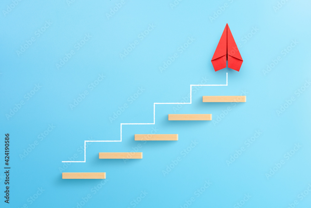 Wooden block stacking as step stair with red paper plane on blue ...