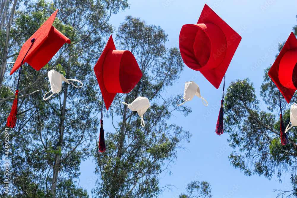 Graduation hats and masks thrown into the air over a blue sky on campus ...