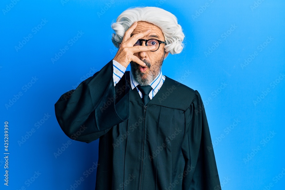 Middle age hispanic man wearing judge uniform peeking in shock covering ...