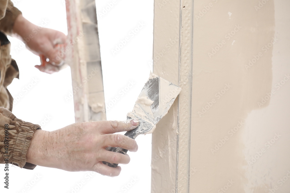 Builder using a trowel to add plaster. Plastering wall with putty-knife ...