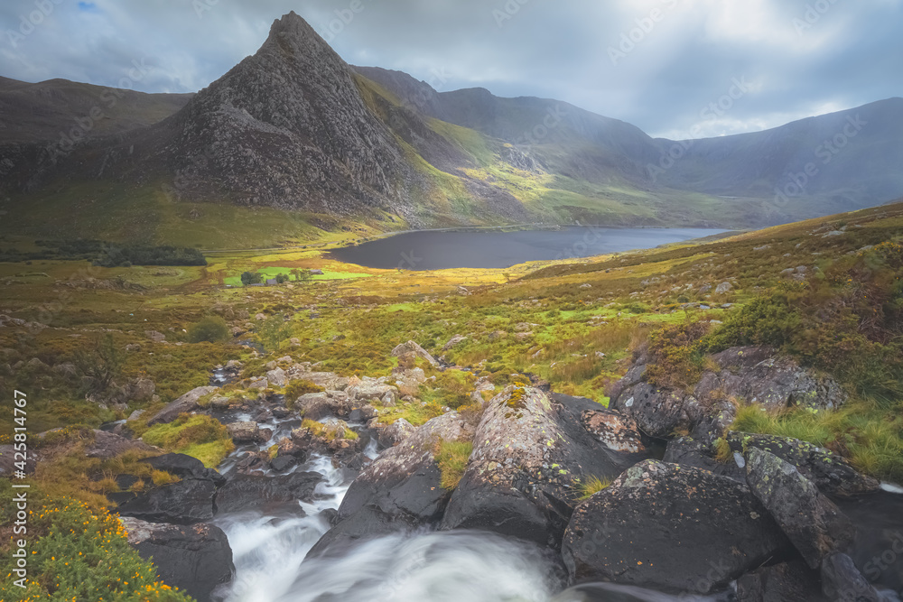Moody, dramatic landscape of mountain stream and light rays beaming ...