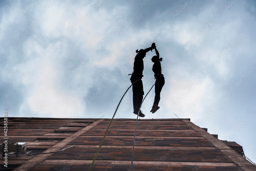 Two person silhouettes, dancing in the air, tied by the ropes on the ...